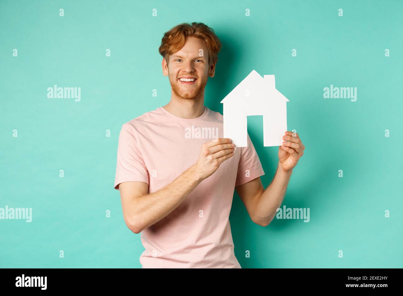 Real estate concept. Young man with red hair, wearing t-shirt, showing ...