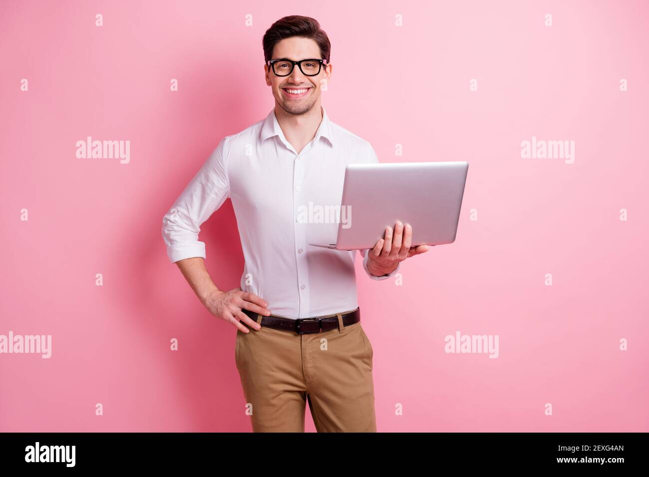 Photo of young man put hand on waist hold netbook toothy smile eyewear ...
