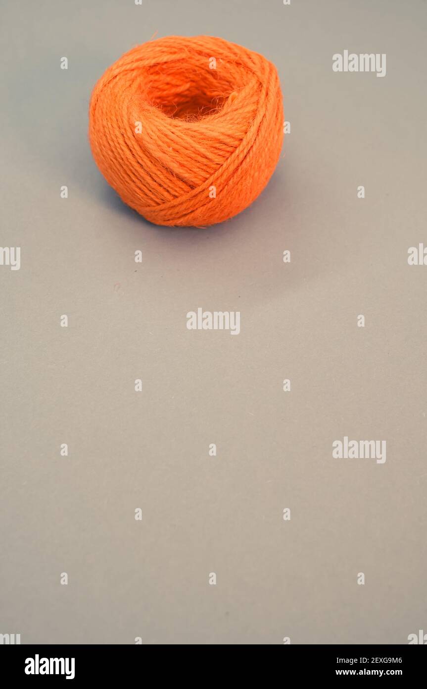 A vertical shot of an orange thread yarn isolated on a grey background ...