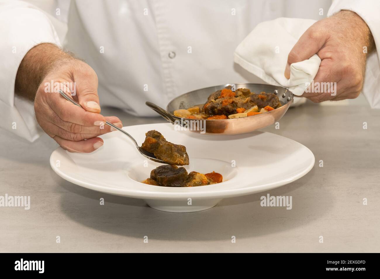 Selective focus of a male chef using a spoon to arrange beef on a plate ...
