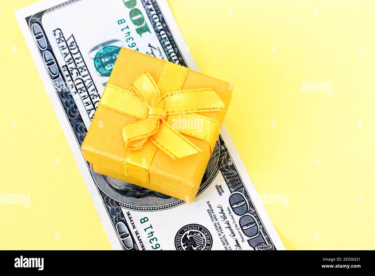 Hundred dollar bill and yellow jewelry gift box on pale yellow ...