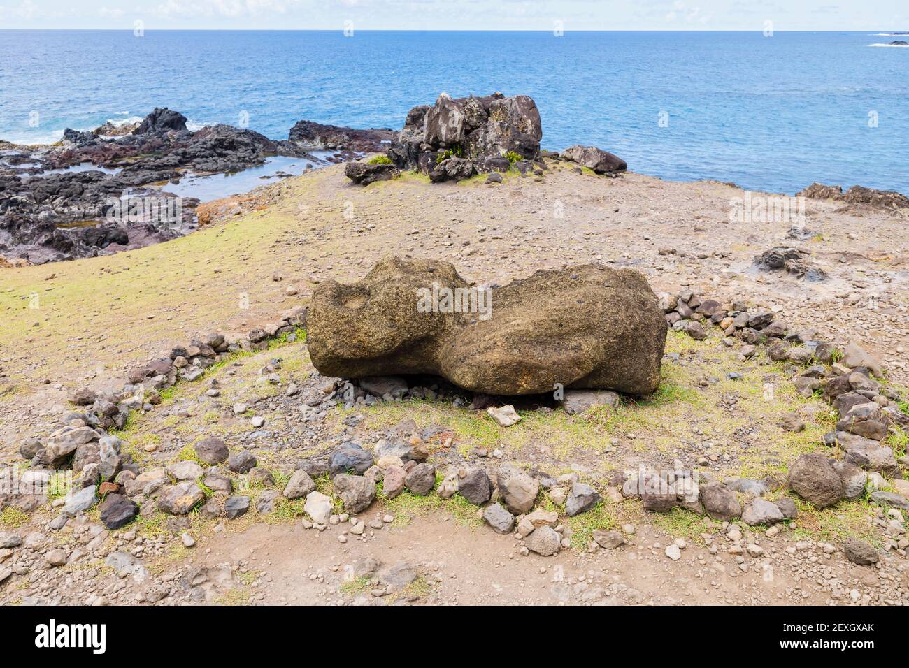 A weathered toppled moai laying on the ground in a ring of stones and ...