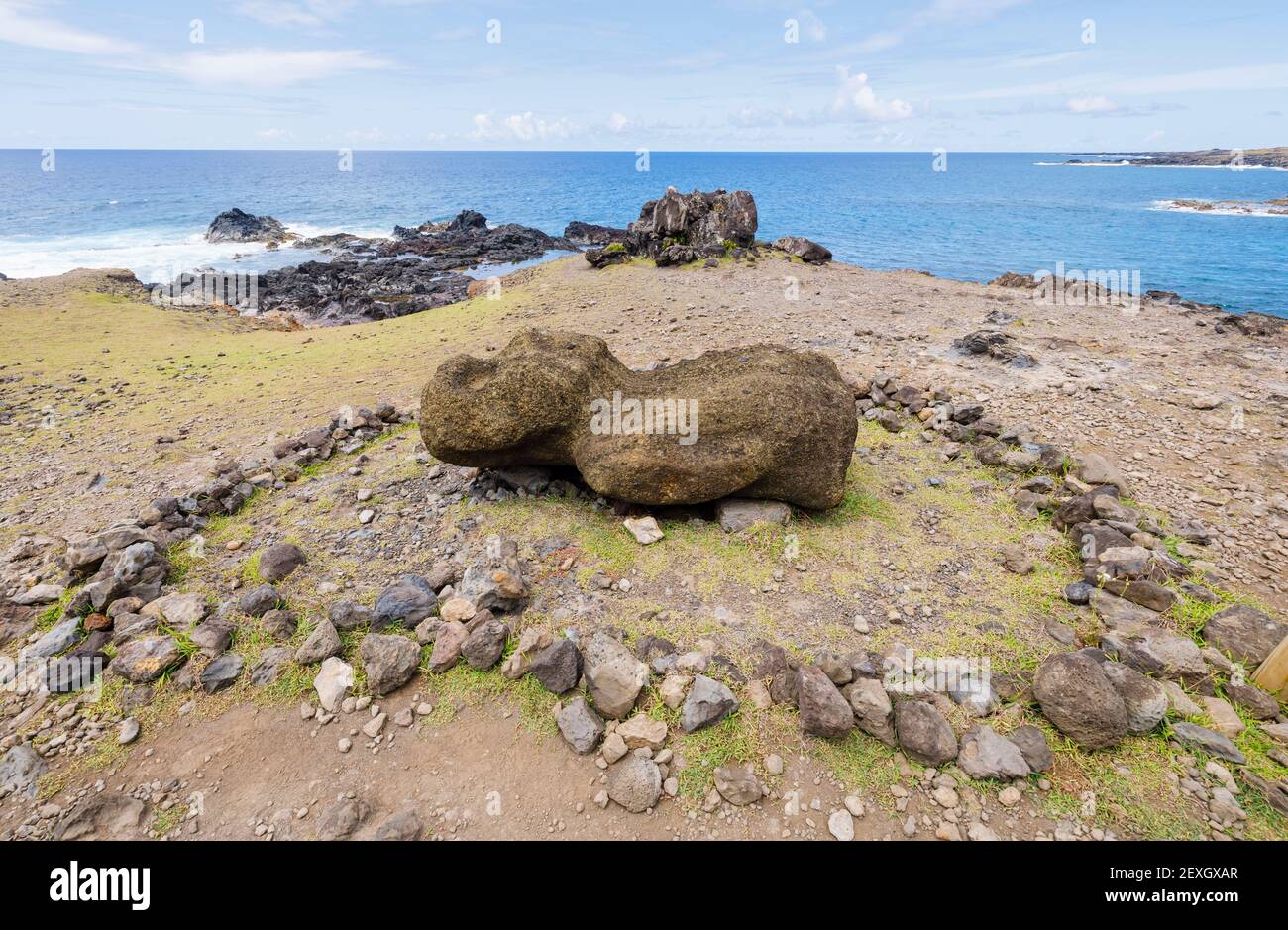 A weathered toppled moai laying on the ground in a ring of stones and ...