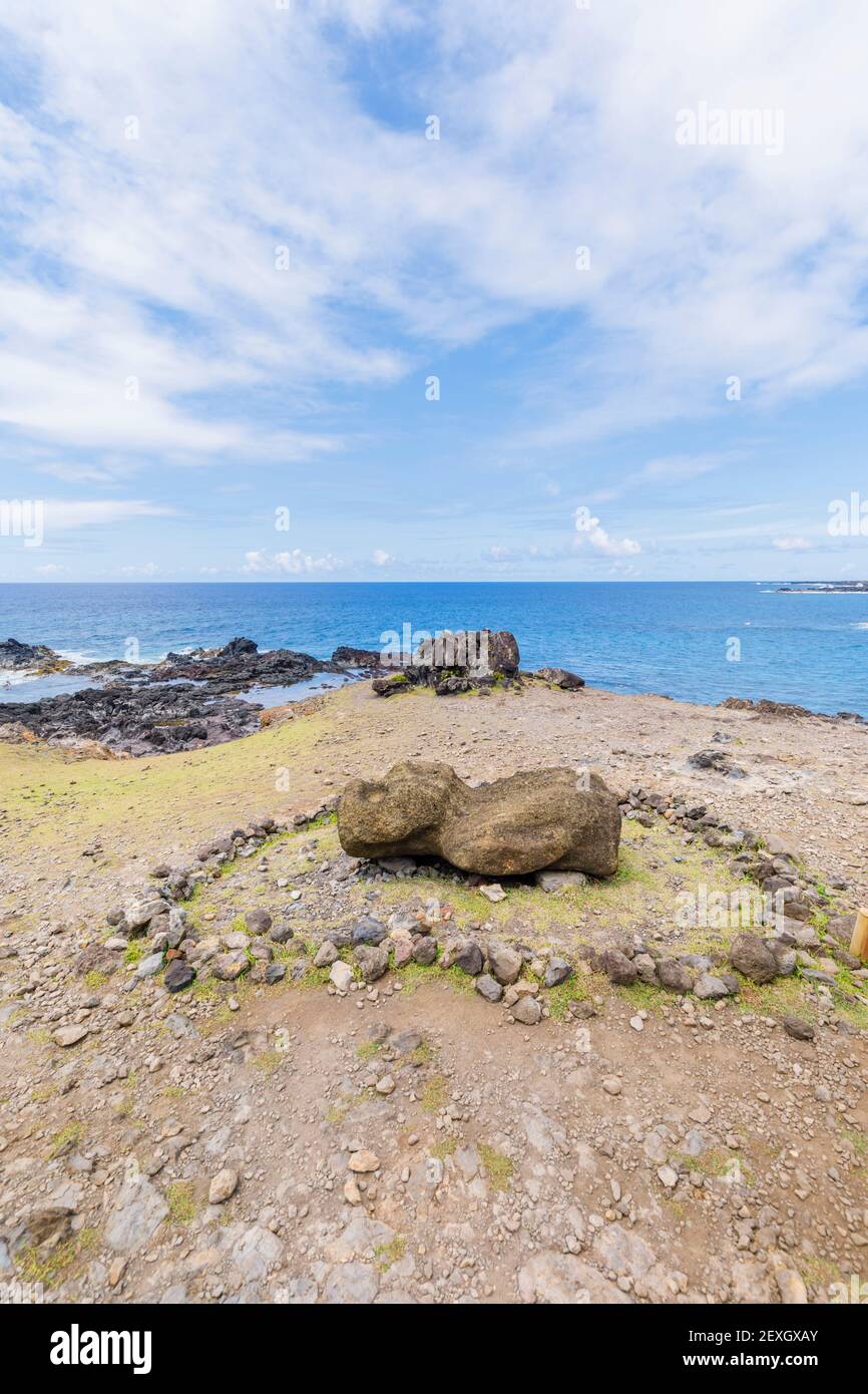 A weathered toppled moai laying on the ground in a ring of stones and ...
