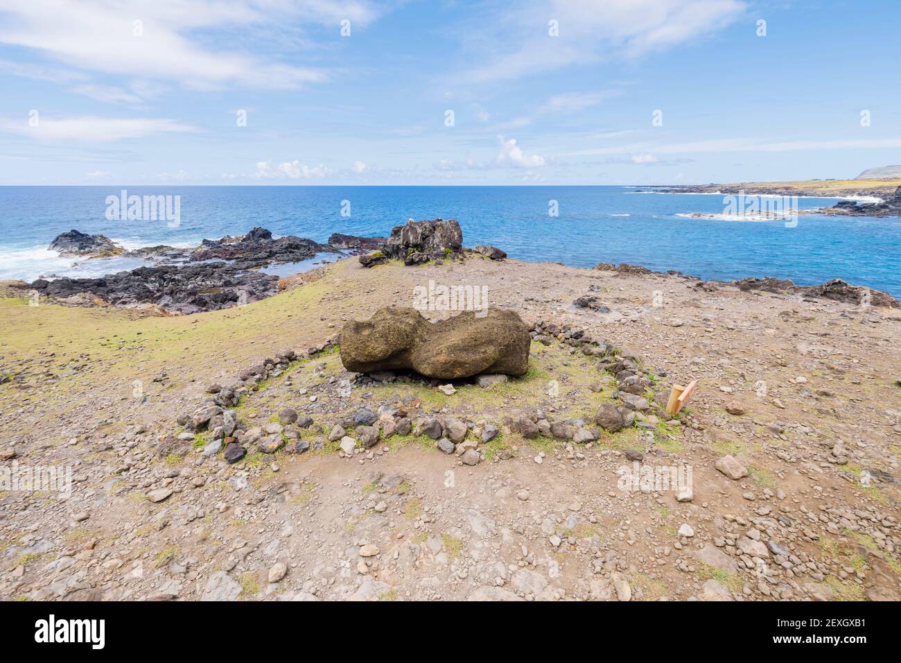 A weathered toppled moai laying on the ground in a ring of stones and ...