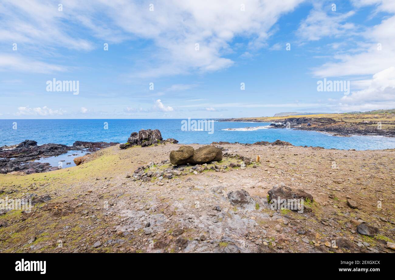 A weathered toppled moai laying on the ground in a ring of stones and ...