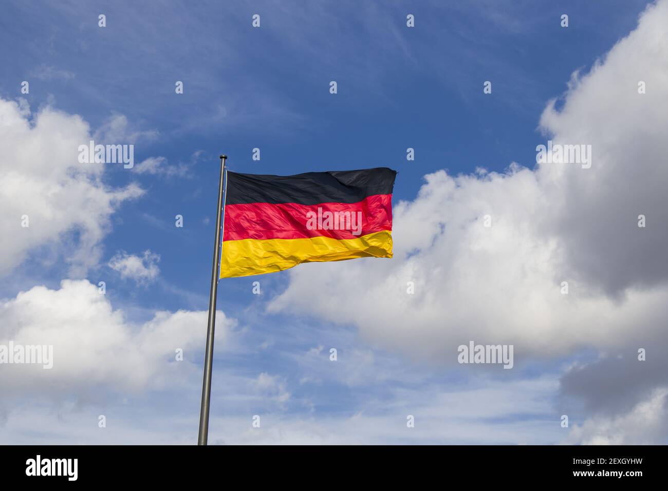 A pole with a waving German flag on the blue cloudy sky background ...