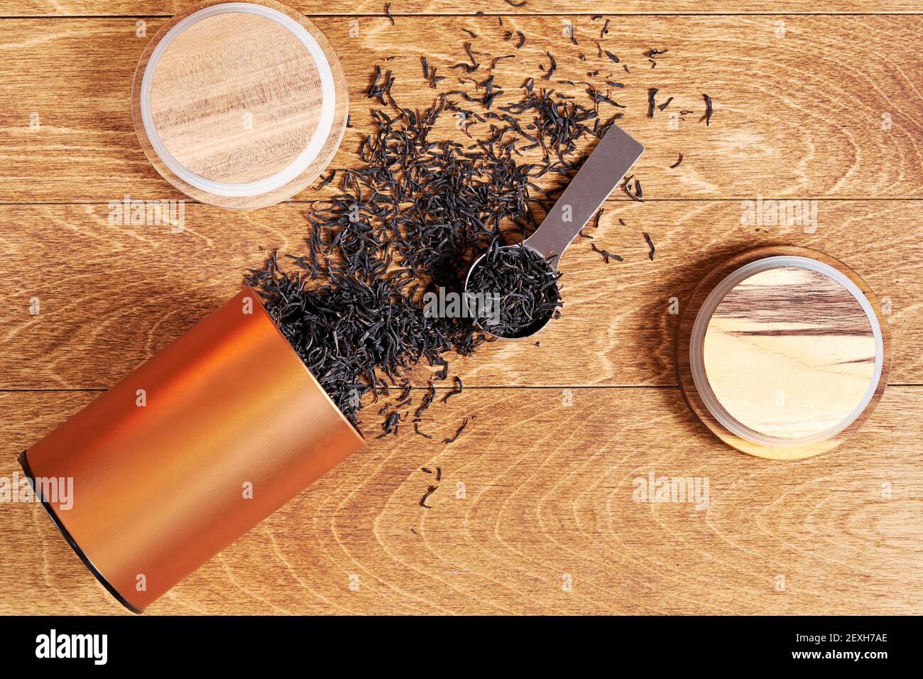 Black tea leaves scattered on the wooden table with jar, spoon and cup ...