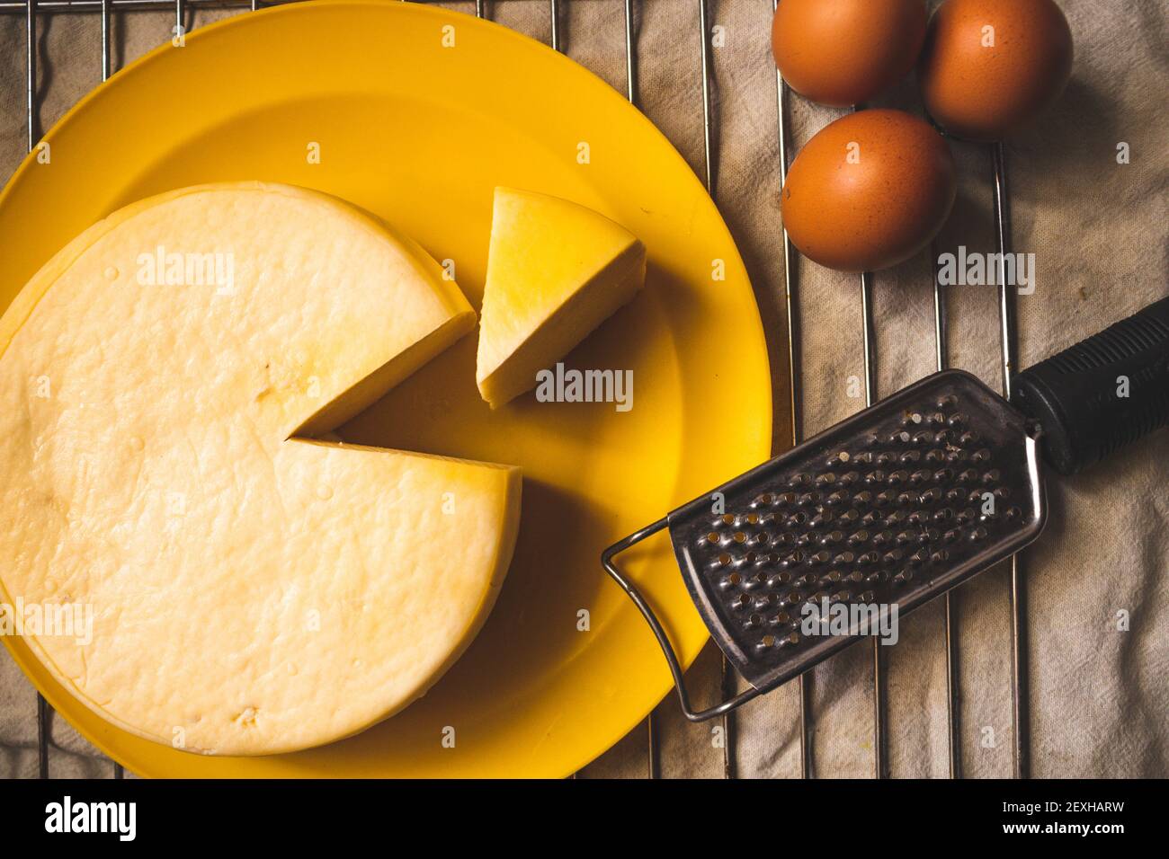A top view of a cut gouda cheese on a plate on the table with eggs and ...