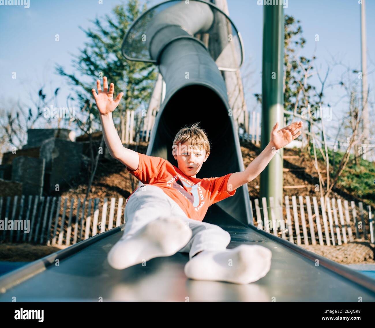 Preteen boy coming out of a tunnel slide with his hands up and no shoes ...