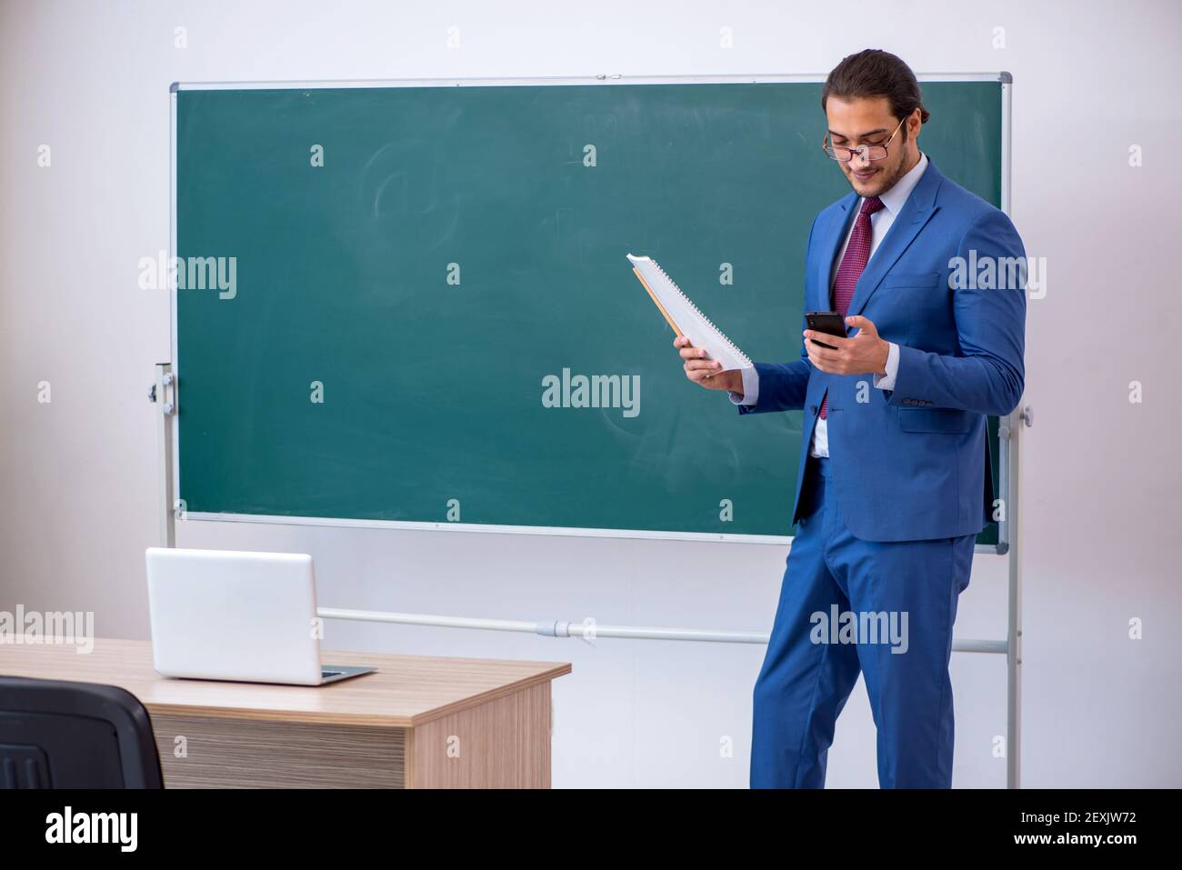 Young teacher in suit in front of green board Stock Photo - Alamy