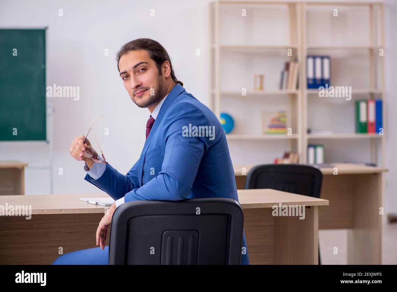 Young teacher in suit in front of green board Stock Photo - Alamy