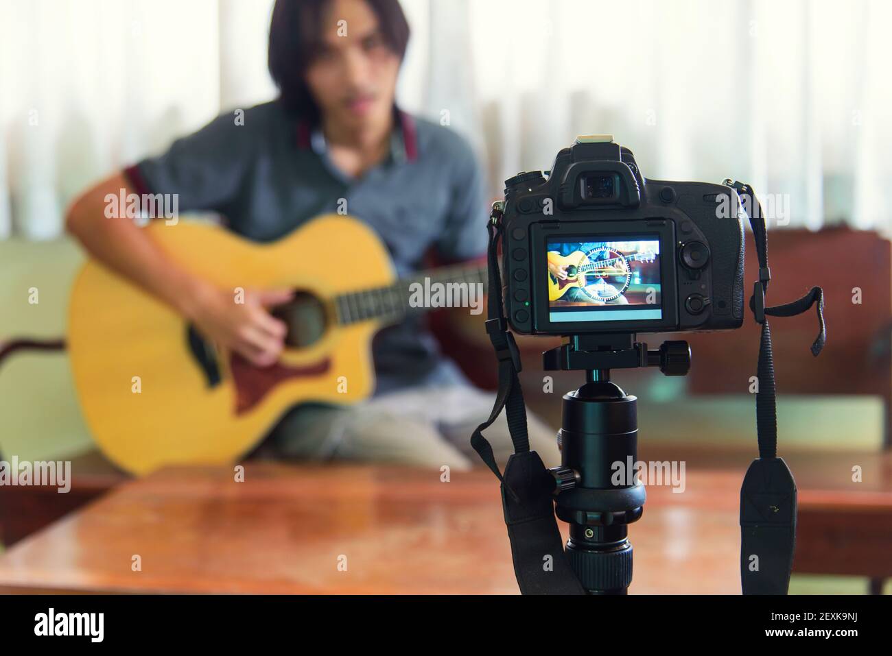 The man recording video clip of his playing guitar by camera on tripod ...
