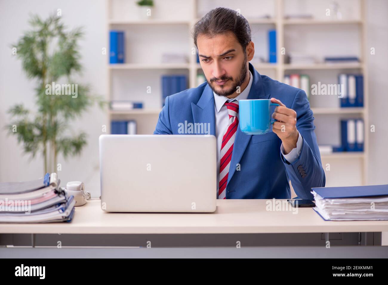 Young employee drinking coffee at workplace Stock Photo - Alamy