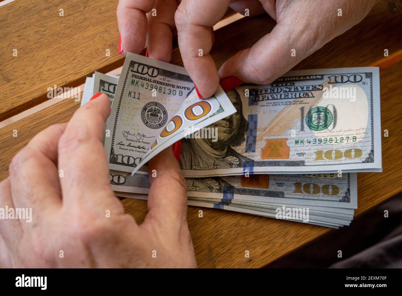 A closeup of a person counting cash dollar bills on a wooden surface ...