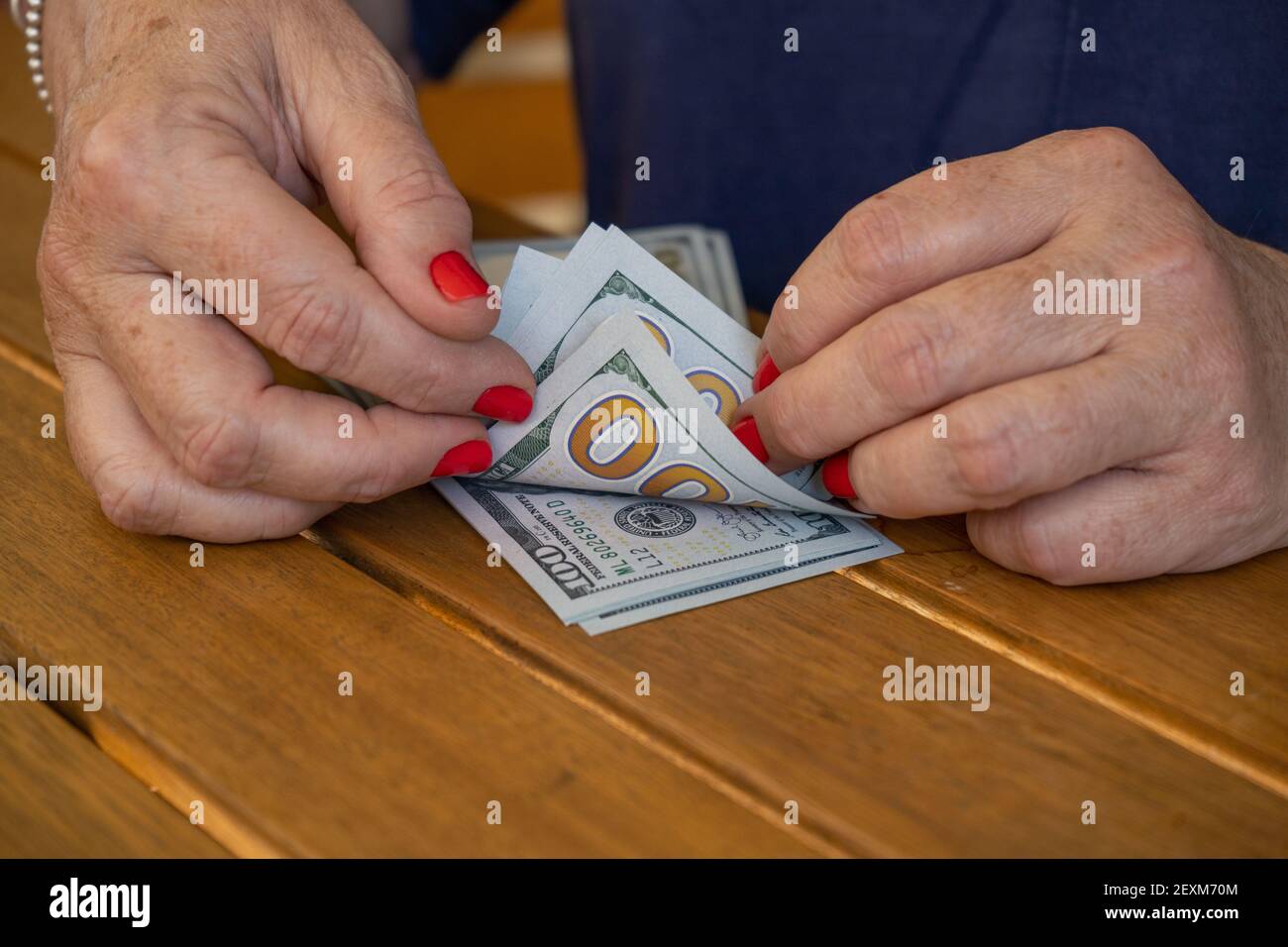 A closeup of a person counting cash dollar bills on a wooden surface ...