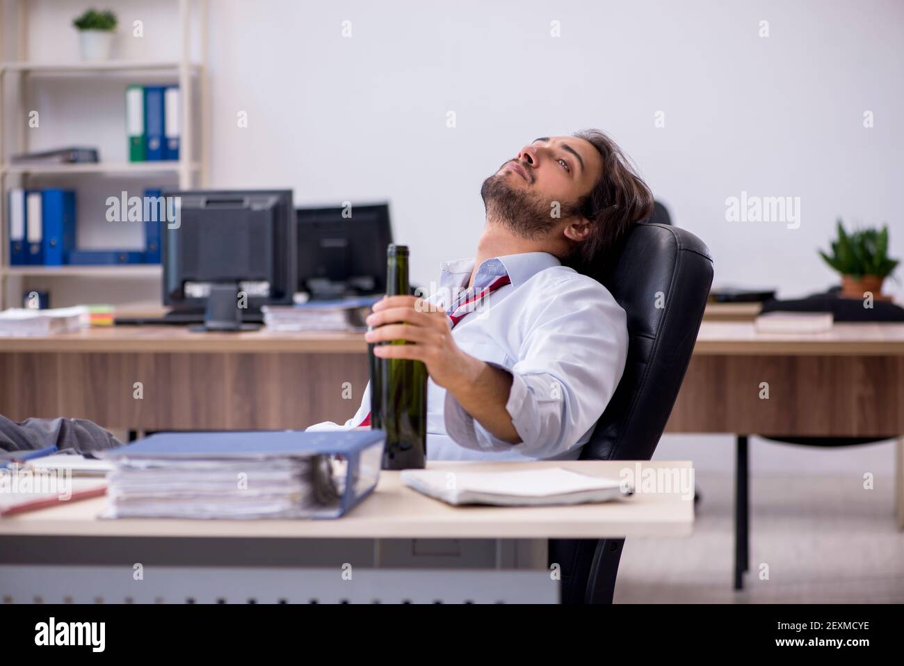 Young male employee drinking alcohol at workplace Stock Photo - Alamy