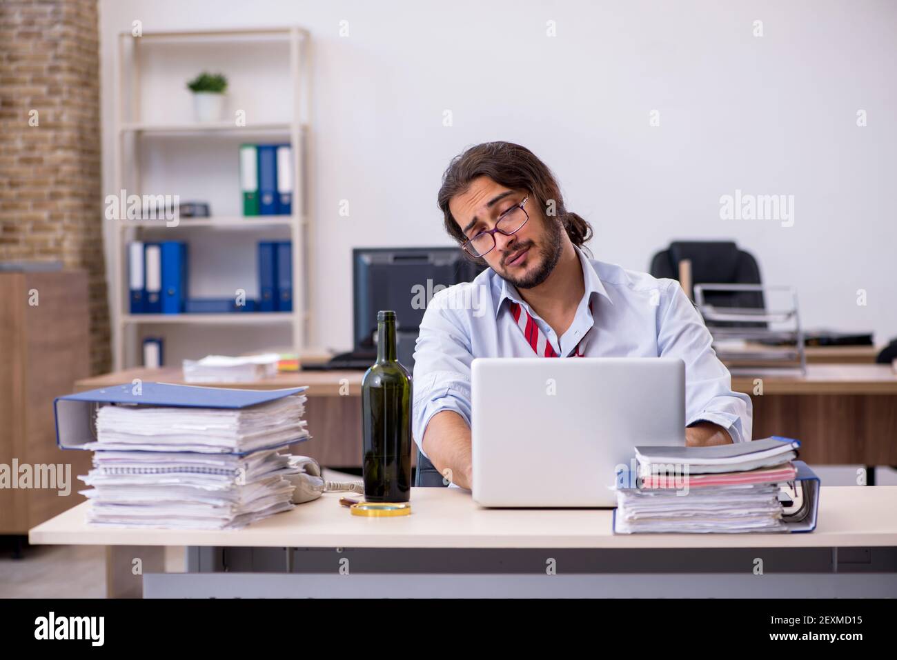 Young male employee drinking alcohol at workplace Stock Photo - Alamy
