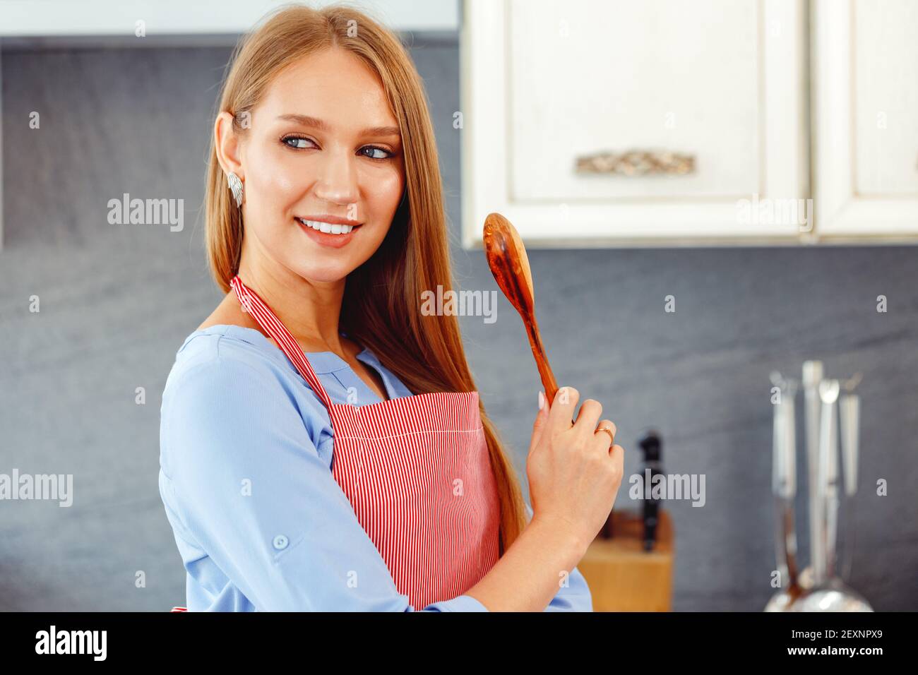 Young woman holding wooden spoon in kitchen Stock Photo - Alamy