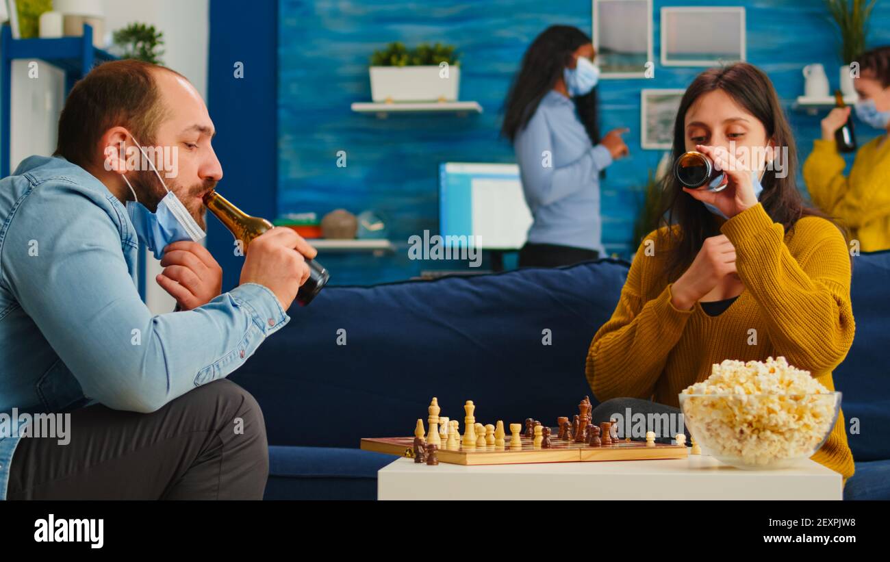 Group of friends with protection masks playing chess while drinking ...