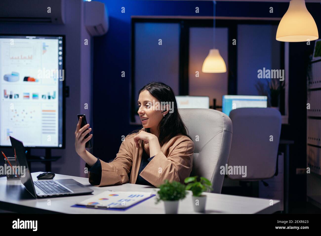 Freelancer talking during virtual meeting at midnight in empty working place. Woman working on ...
