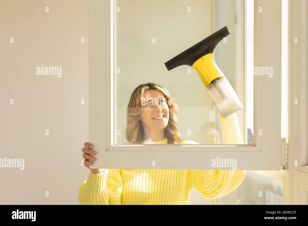 smiling young girl with window cleaning equipment stands outside window ...