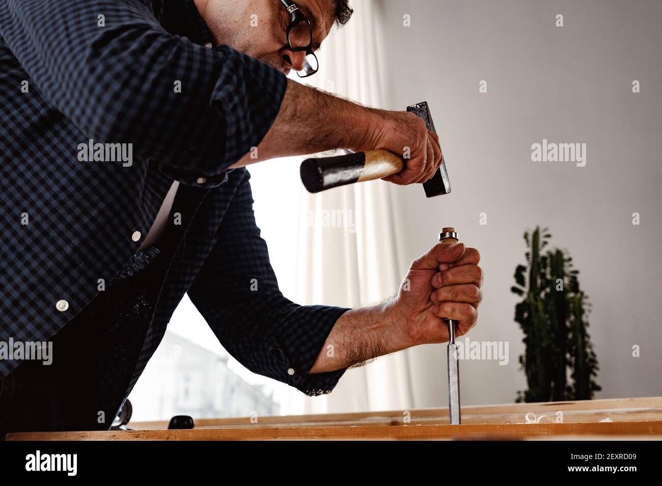 Middle-aged man carpenter working in a workshop with chisel and hammer ...