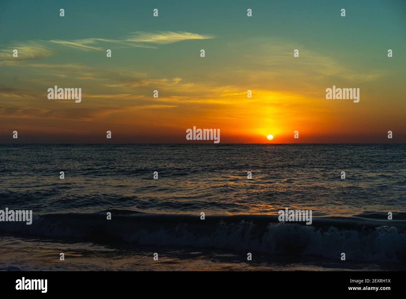 Rising sun on the horizon above ocean or sea. On the blue sky and ...