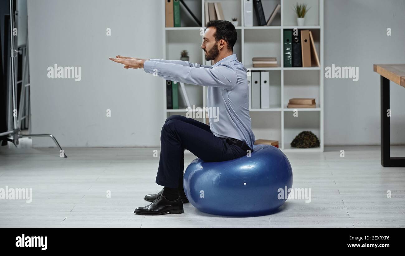 Side view of businessman working out on fitness ball in office Stock ...