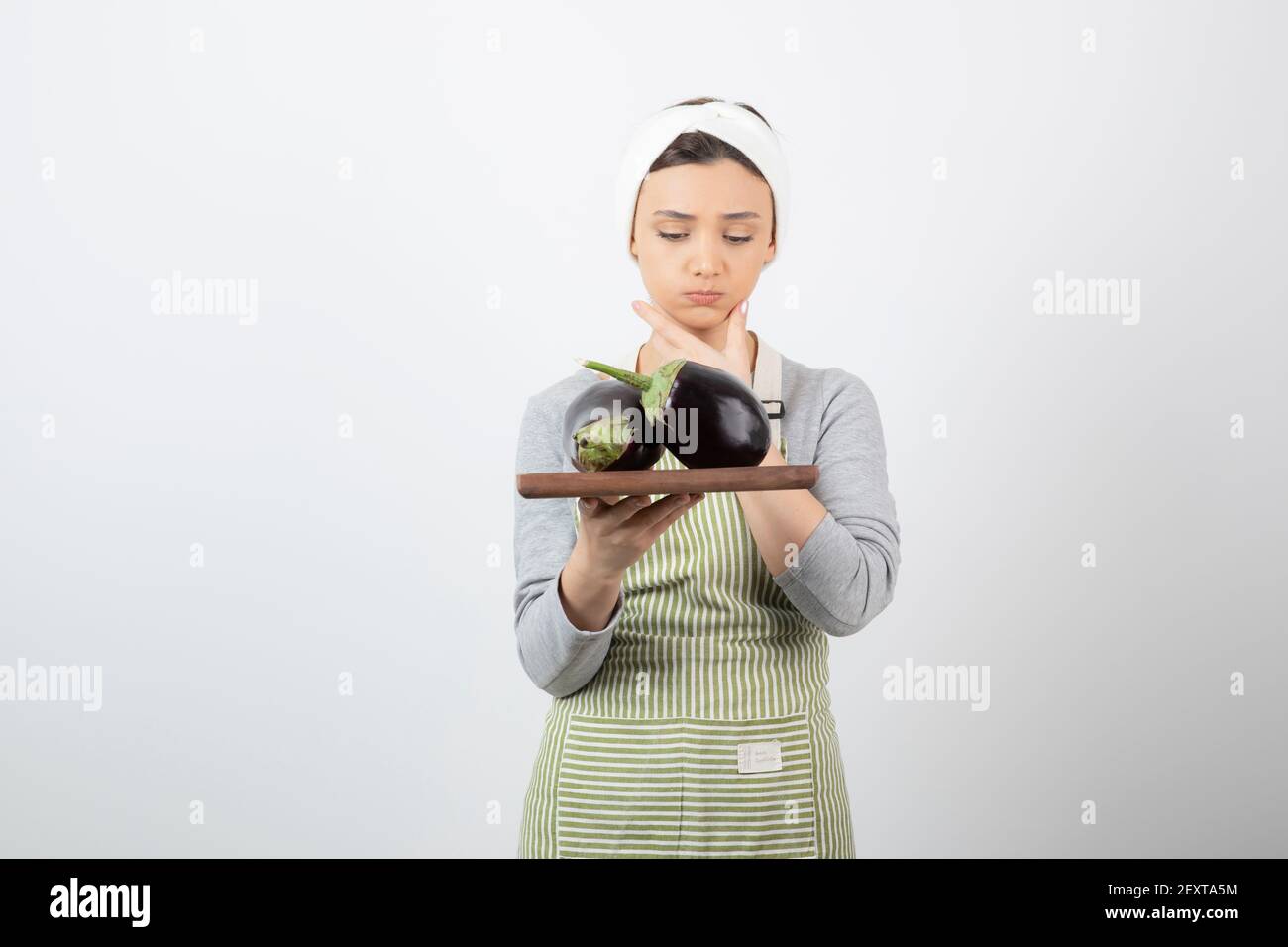Portrait of female cook looking at plate of big eggplants on white ...