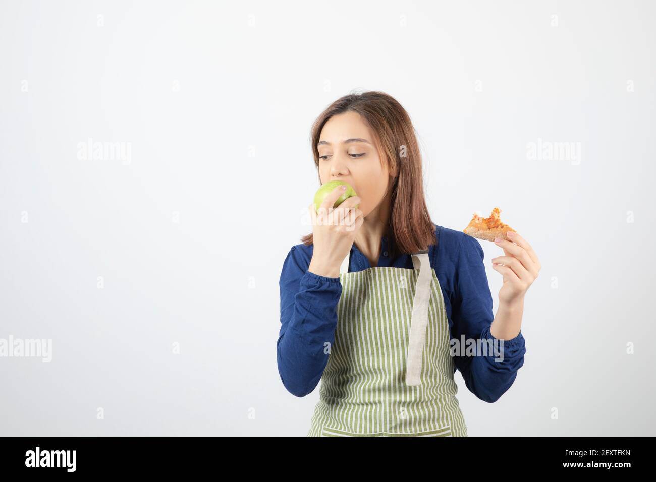 Adorable young girl in apron eating green apple instead of pizza Stock ...