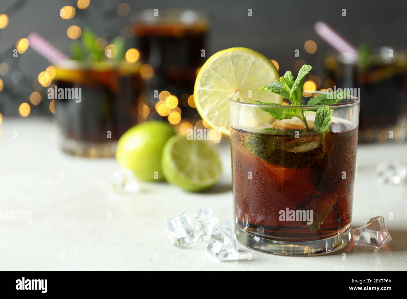Glass of Cuba Libre on white textured table against blurred lights ...
