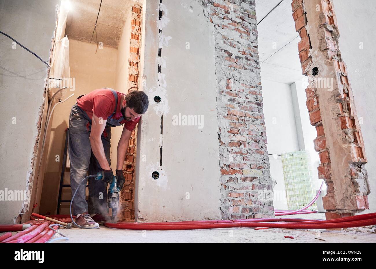 Bearded young plumber in work overalls using electric drill while ...