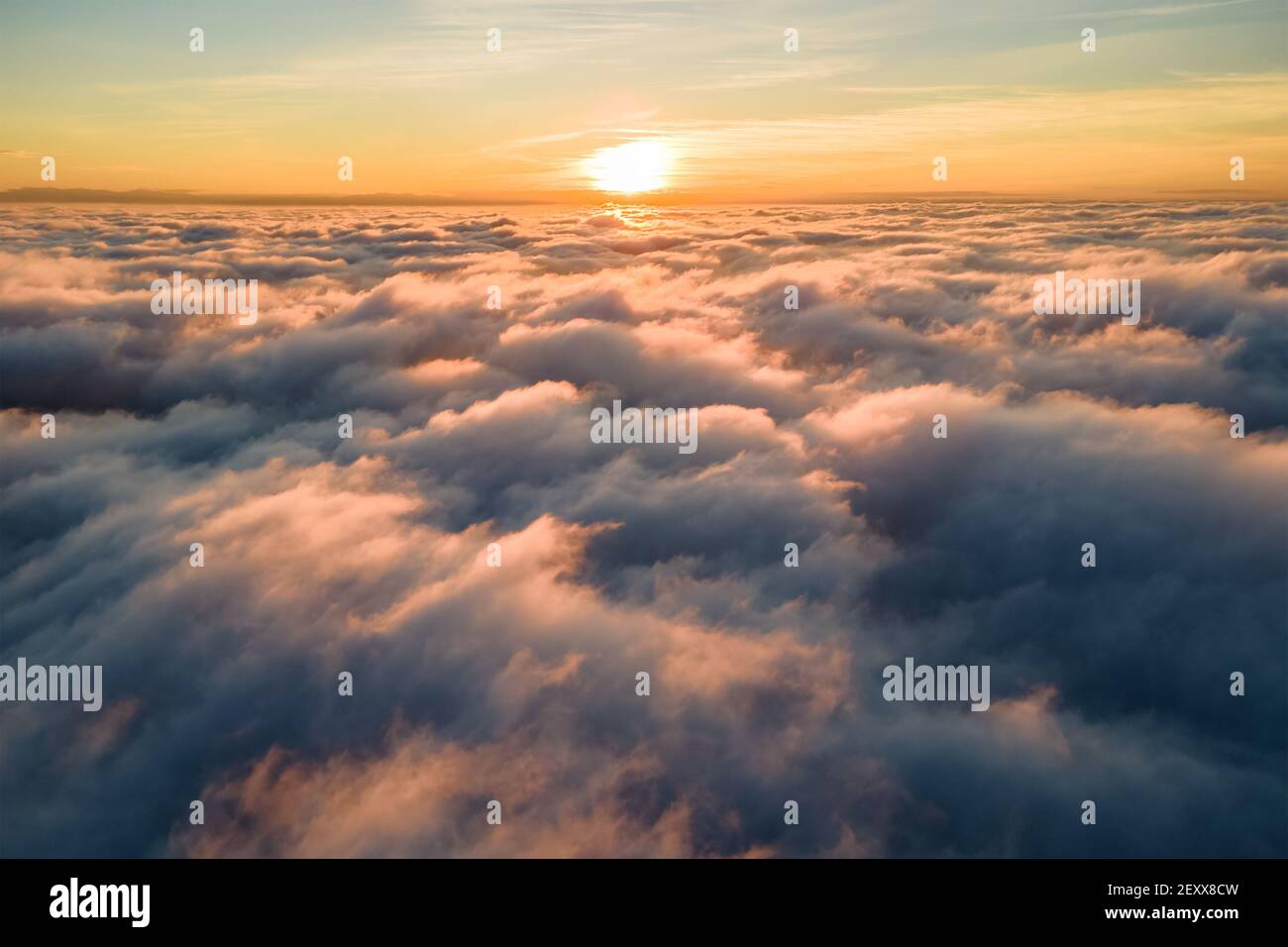 Aerial view of bright yellow sunset over white dense clouds with blue ...