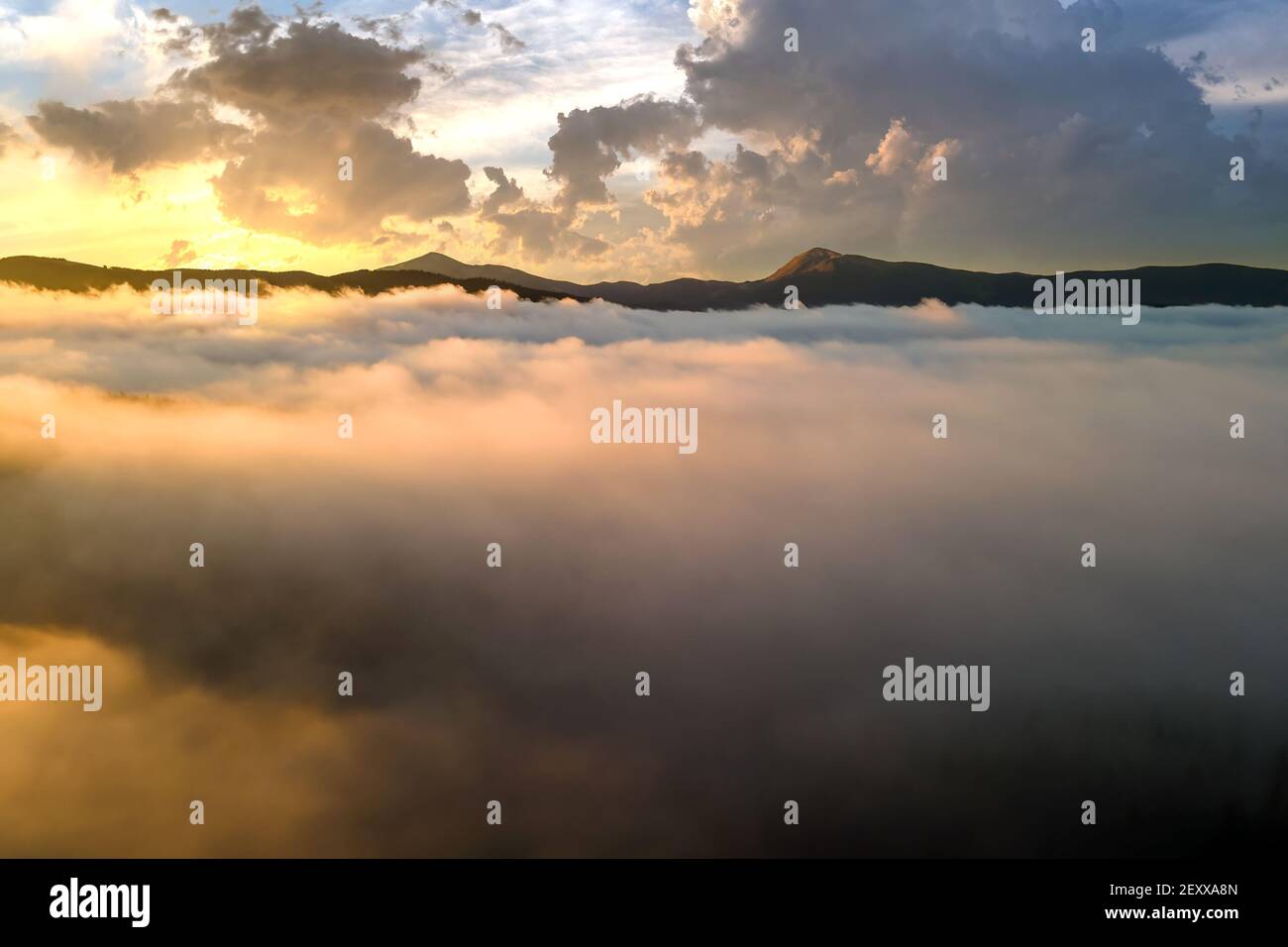 Aerial view of vibrant sunset over white dense clouds with distant dark ...