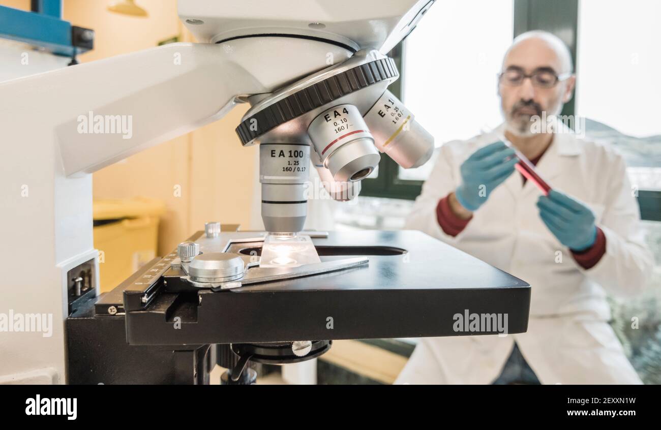 Microscope and male researcher in his 50's in a lab coat with test ...