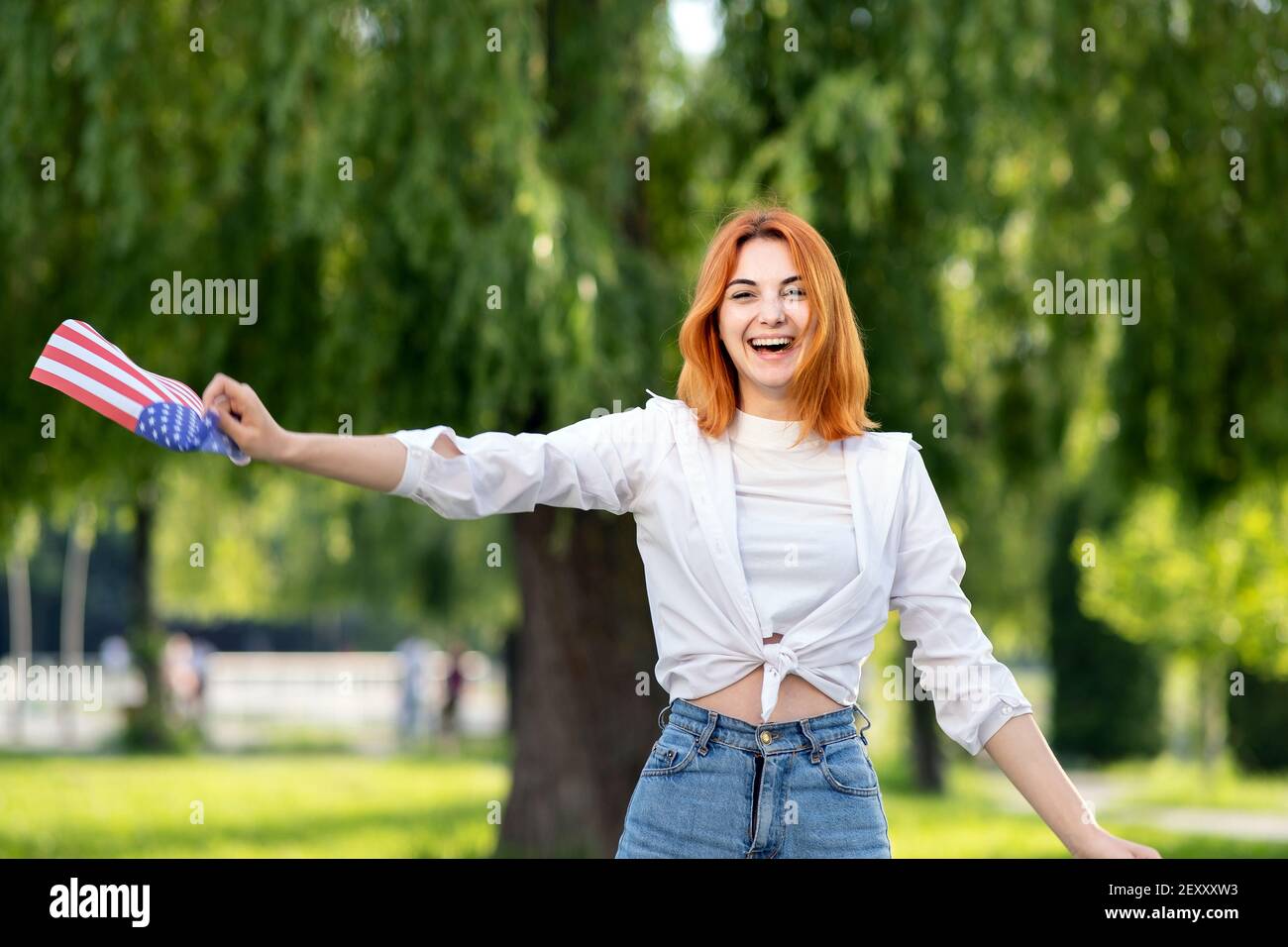Angry young red haired woman protester posing with USA national flag in ...