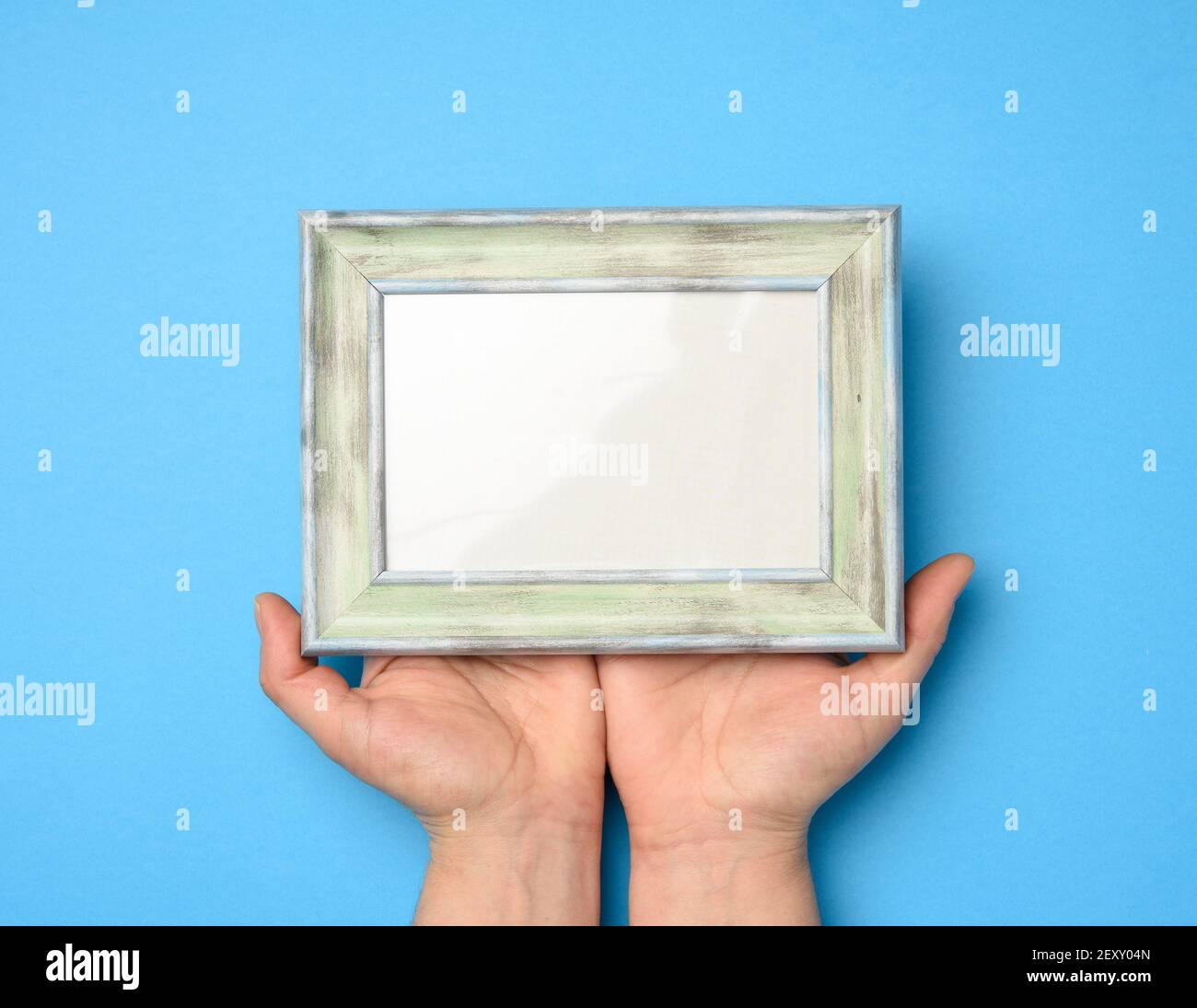 two female hands holding a rectangular blank wooden frame, blue ...