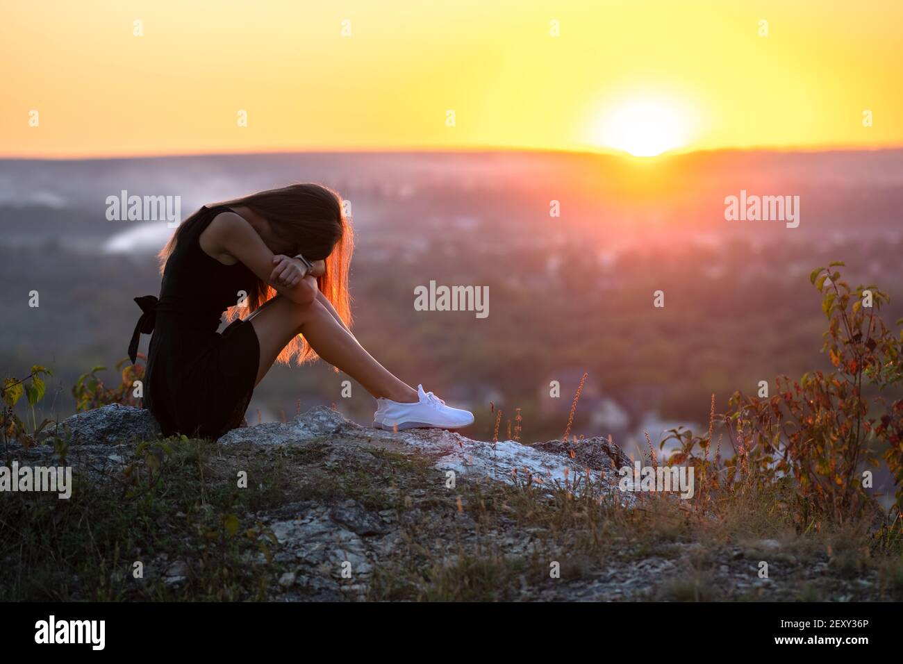 Young depressed woman in black short summer dress sitting on a rock ...