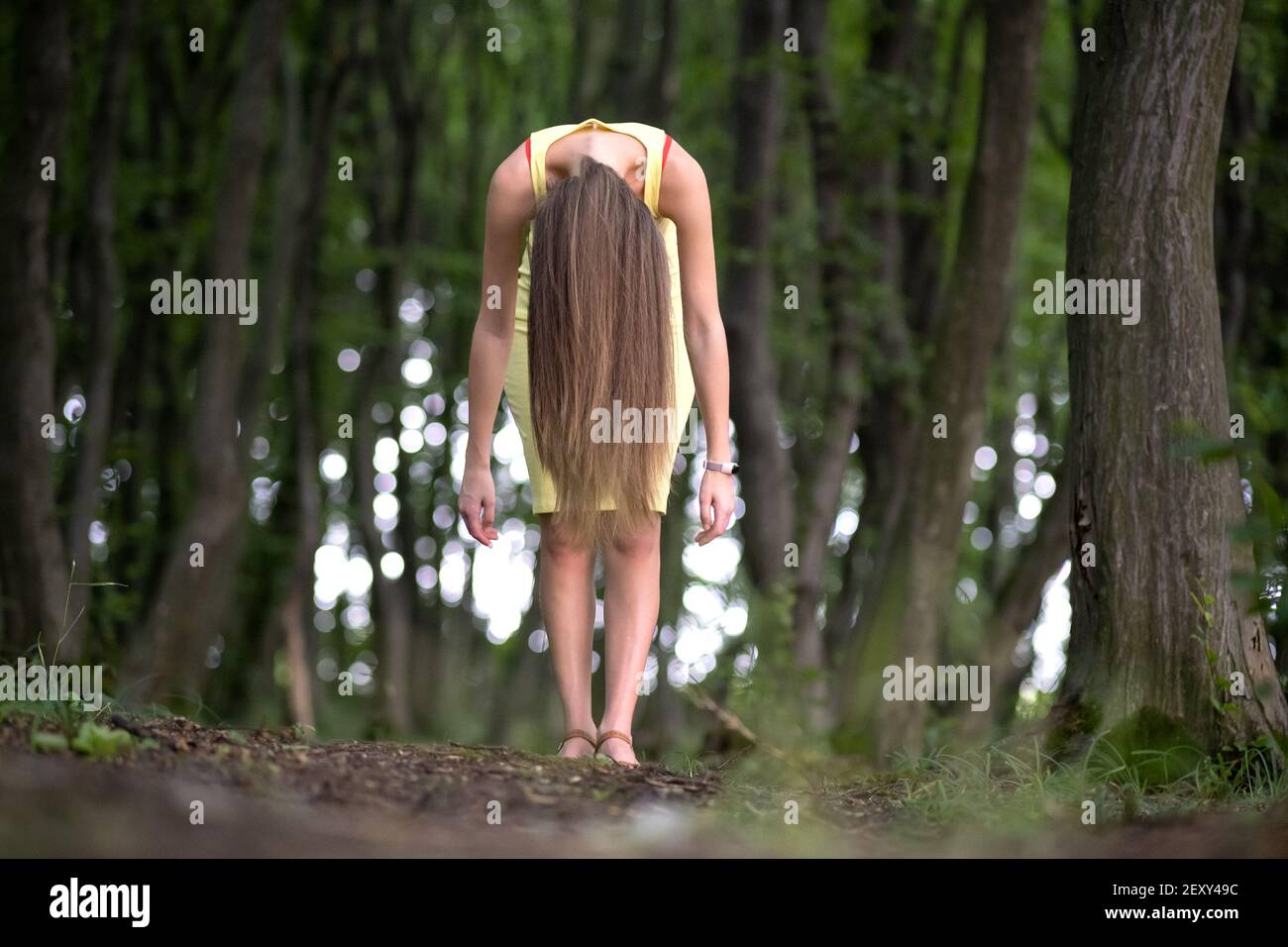 Creepy woman with long hair standing bent down in moody dark forest ...