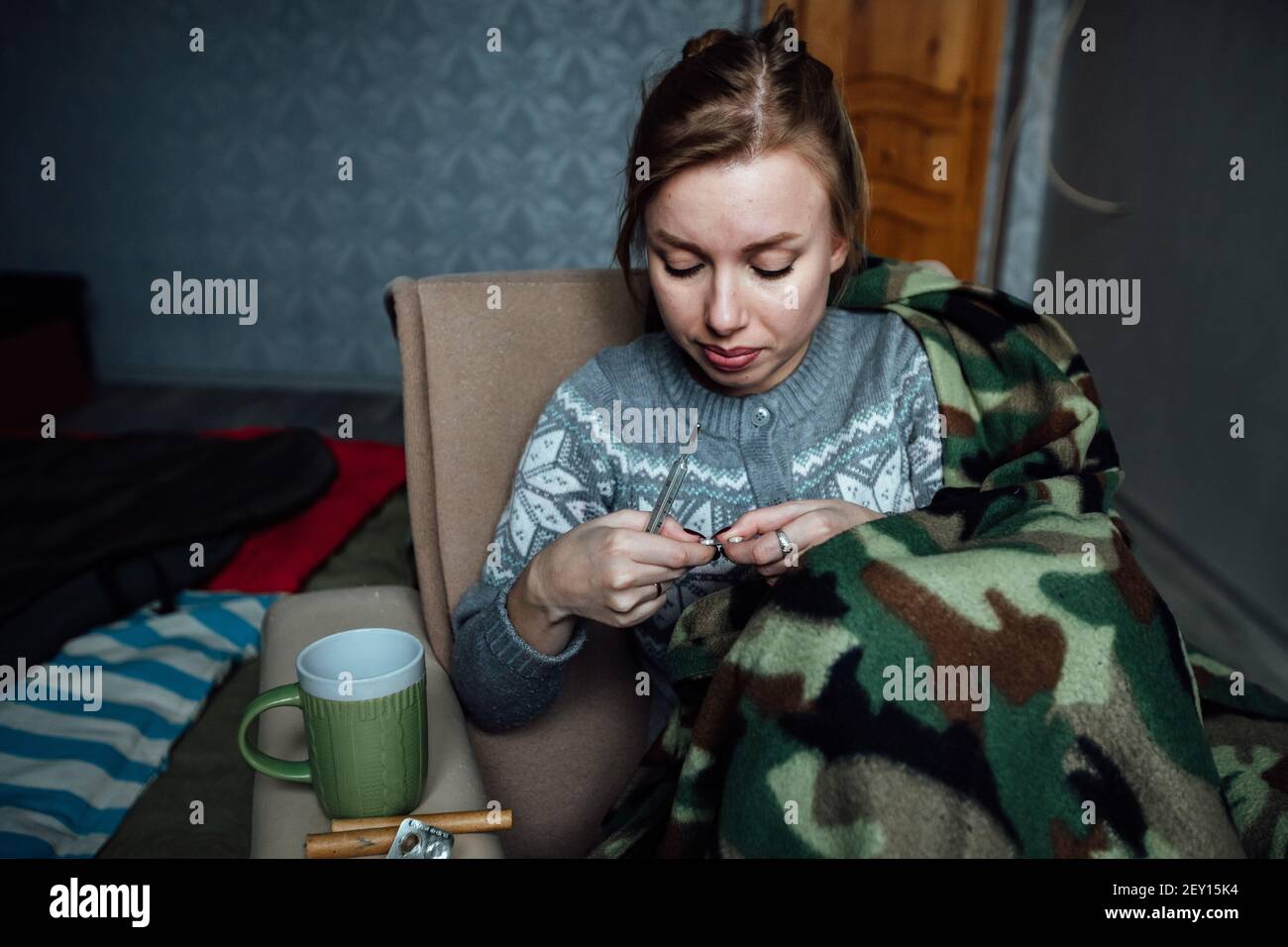 a sick girl sits wrapped in a blanket with a mask on her face. measure ...