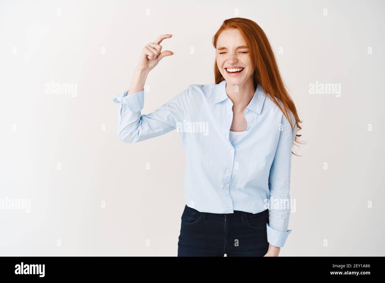 Happy young woman with long red hair showing something small ...