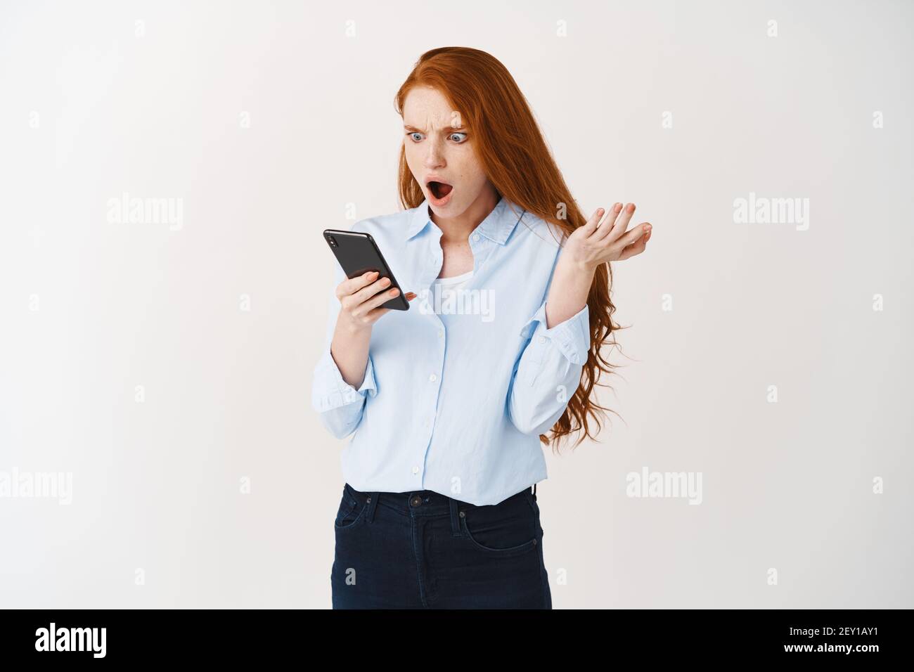 Shocked and angry woman with red hair receive spam on phone, reading ...