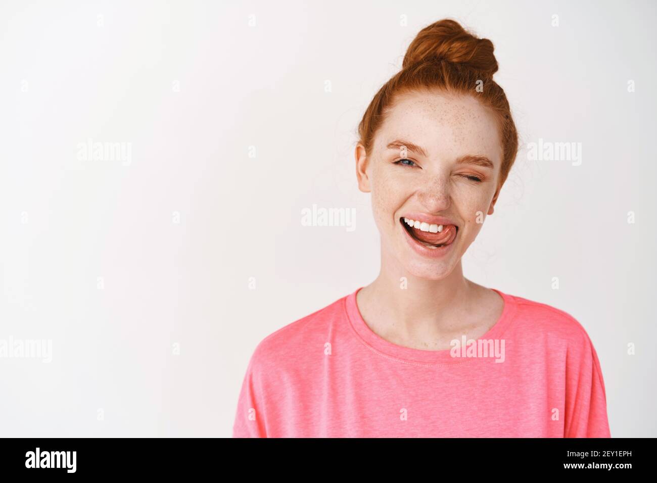Girl with ginger hair combed in messy bun, winking joyfully and showing ...