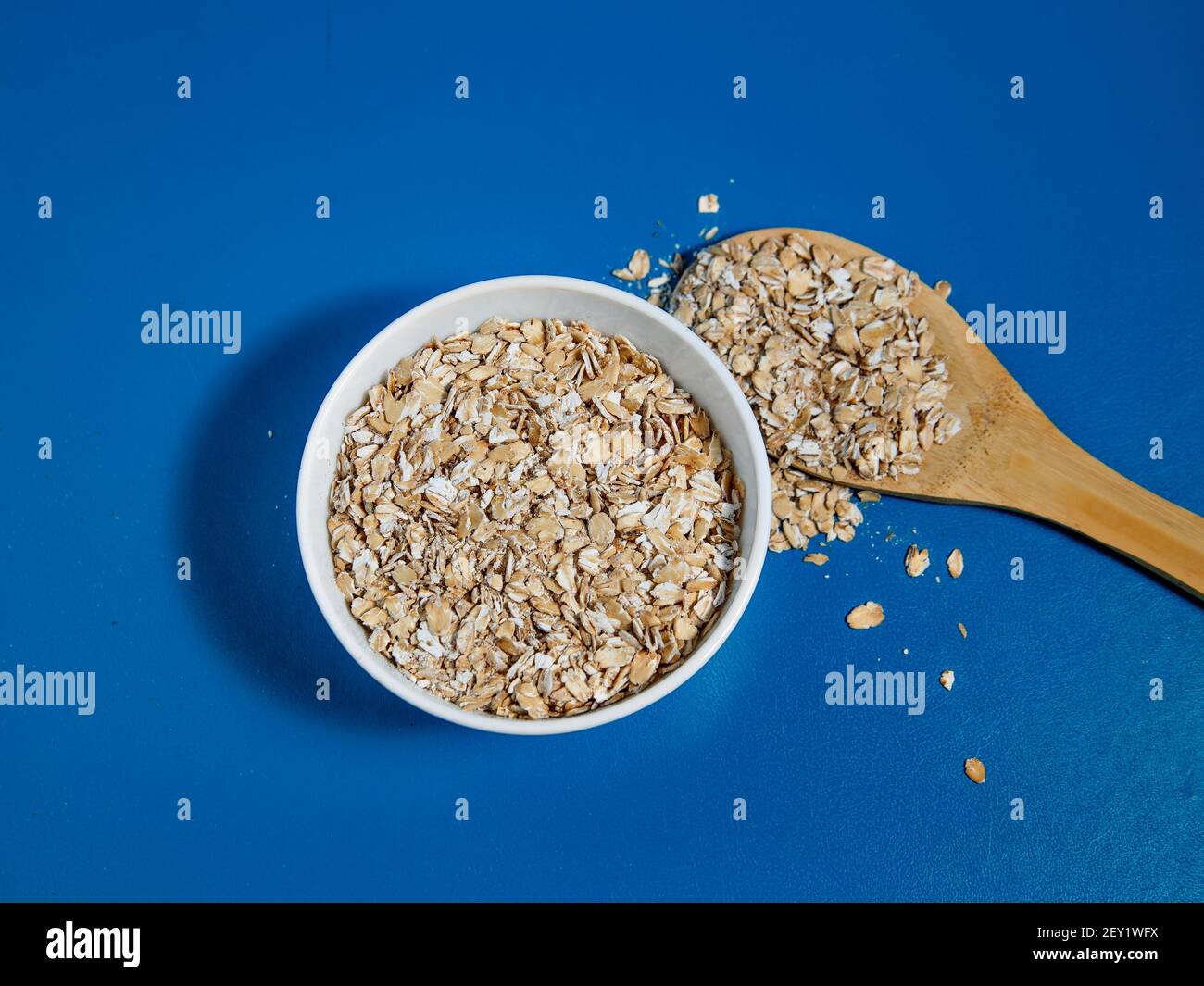 Oatmeal in white plate and wooden spoon on blue surface Stock Photo - Alamy