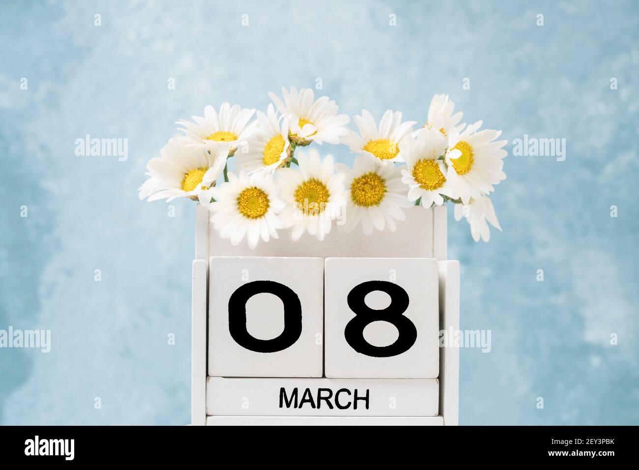White cube calendar for march decorated with daisy flowers over blue ...