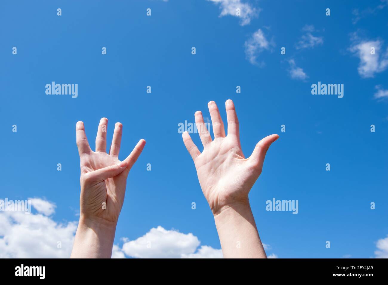 Close-up of female hands showing nine fingers on a blue sky background ...