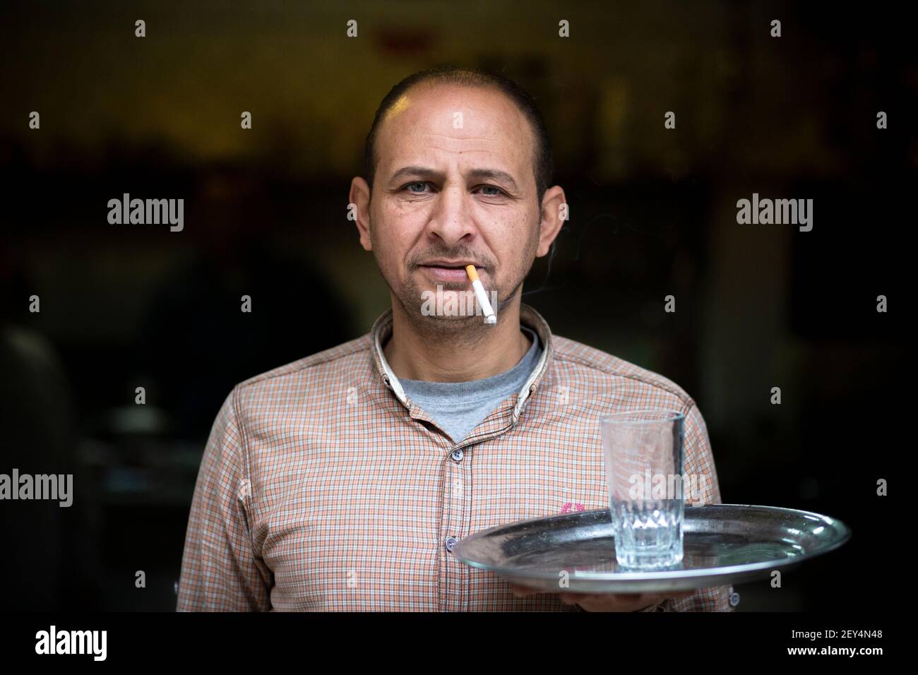 Portrait of a male Egyptian waiter holding a tray and smoking a ...
