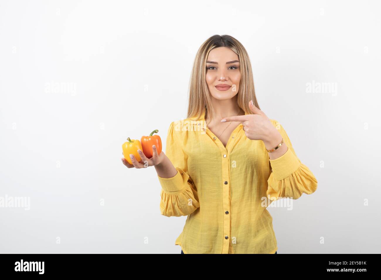 Portrait of blonde woman pointing at colorful bell peppers over white ...