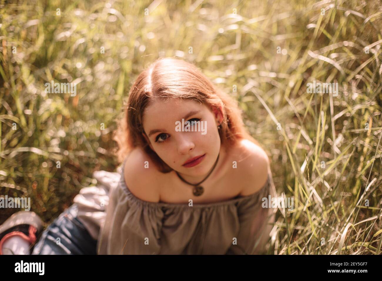 Portrait of teenage girl sitting on field in the grass during summer ...
